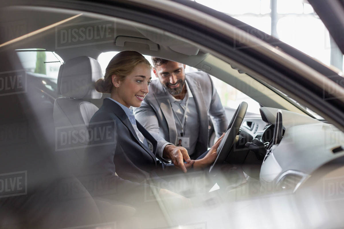 Car salesman explaining new car to female customer in driver’s seat in ...