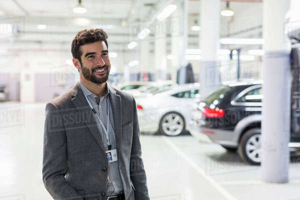 Portrait smiling car salesman looking away in car dealership auto ...