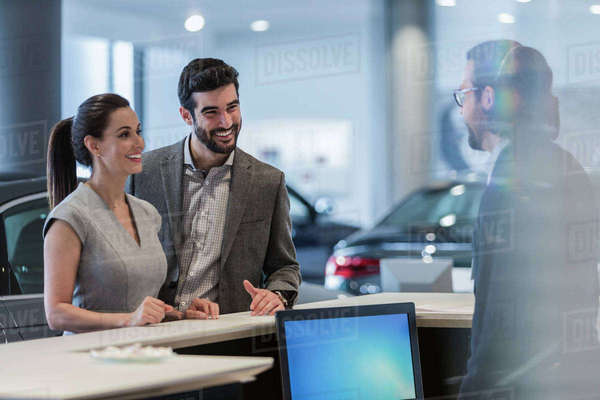 Couple customers talking to receptionist at desk in car dealership ...