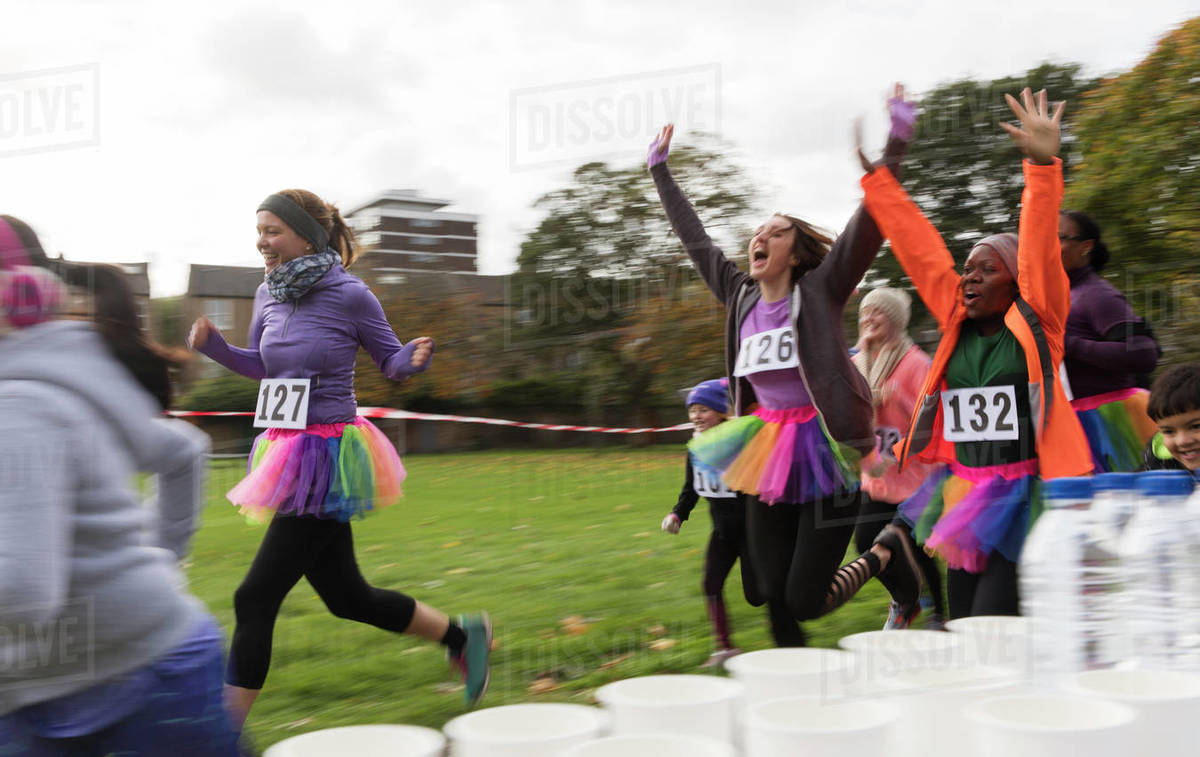 Enthusiastic female runners in tutus cheering, running at charity race ...