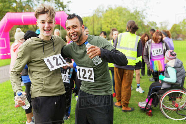 Portrait enthusiastic male runner friends with water hugging at charity ...