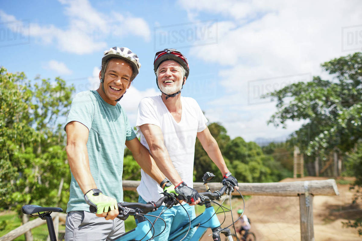 Portrait confident father and son mountain biking on sunny trail ...