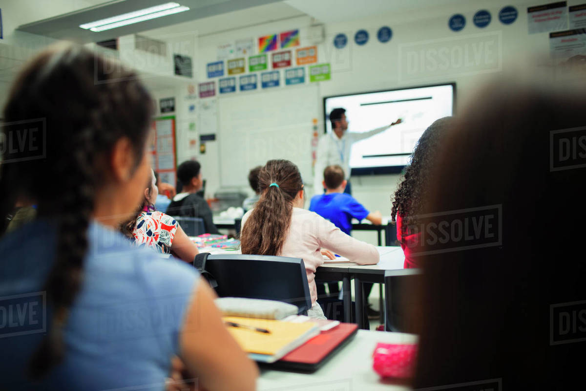 Junior high school students watching teacher give lesson at projection ...