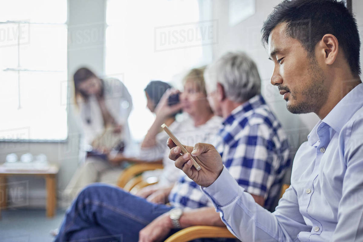 Man using smart phone, waiting in clinic waiting room - Royalty-free ...