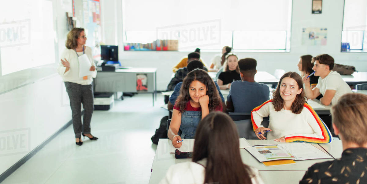 High school girl students talking at table in classroom during lesson ...