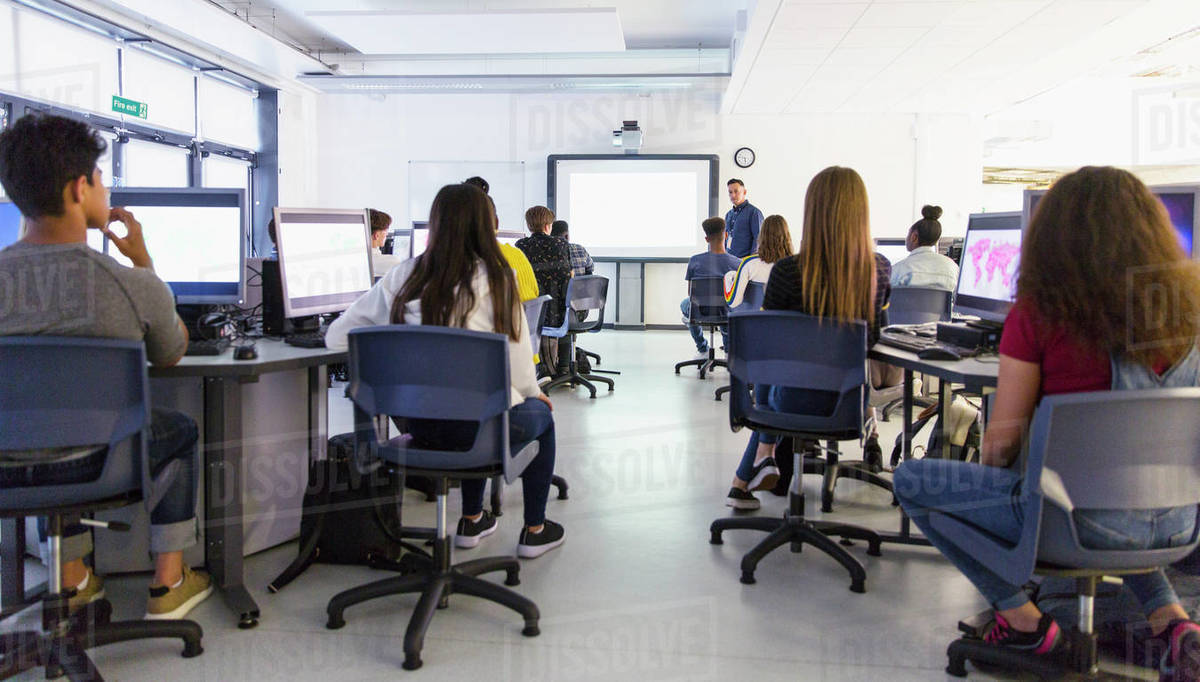 Junior high students at computers watching teacher at projection screen ...
