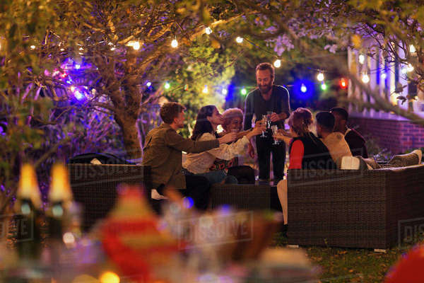Friends drinking under trees with string lights at garden party ...