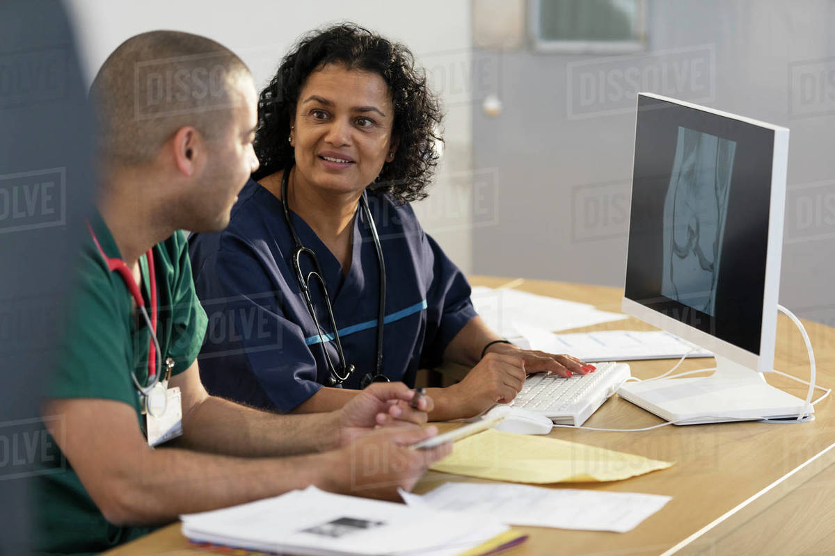Doctors looking at digital x-ray on computer in doctors office ...