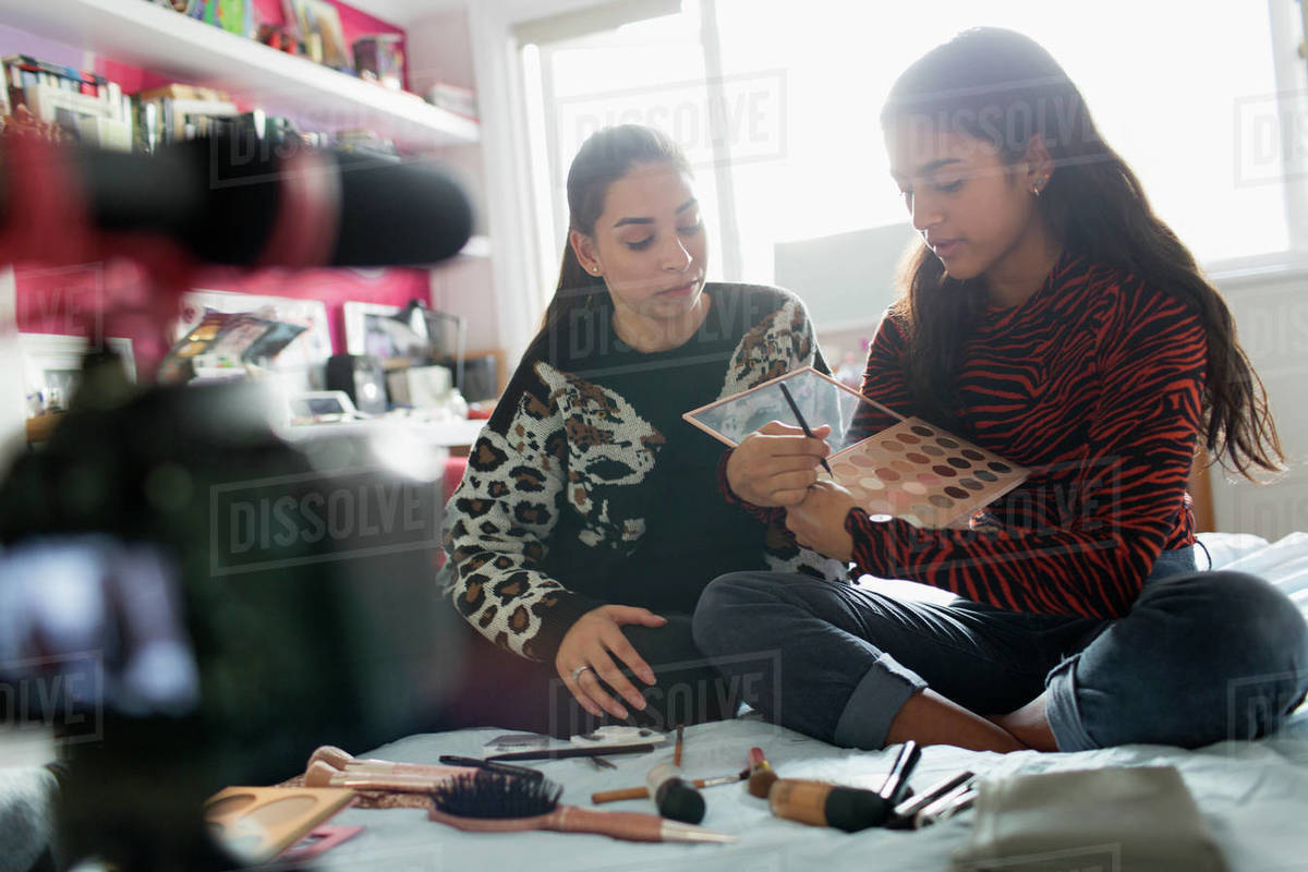 Teenage girls vlogging, demonstrating makeup application on bed ...