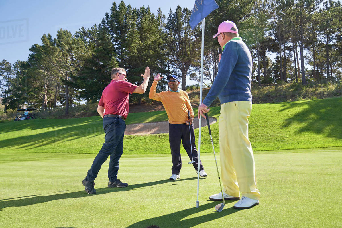 Male friends high fiving on sunny golf course putting green - Royalty ...