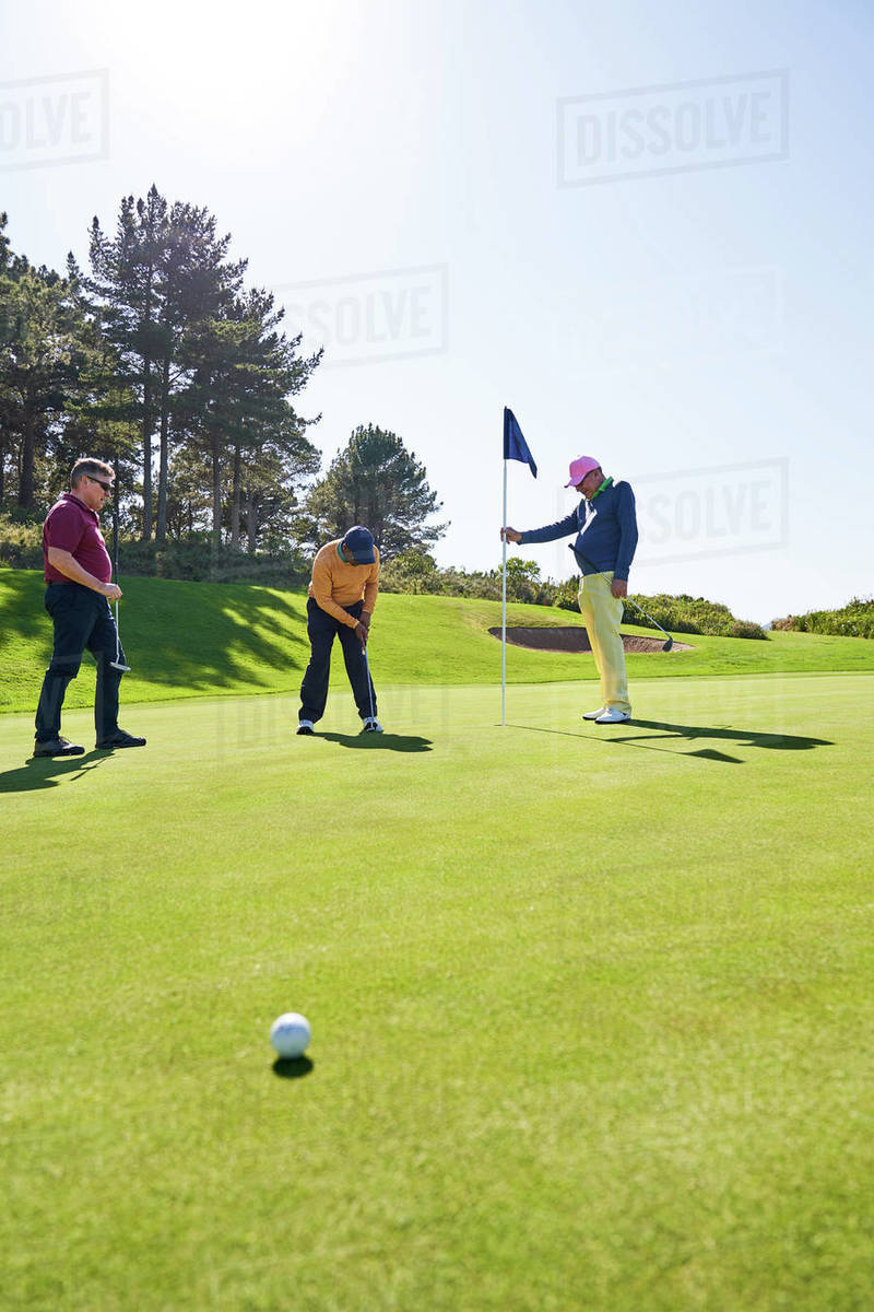 Male golfer putting at hole on sunny golf course putting green ...