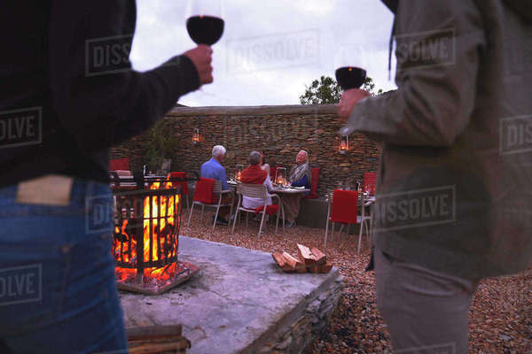 Couple and senior friends dining drinking wine on patio with fire pit ...