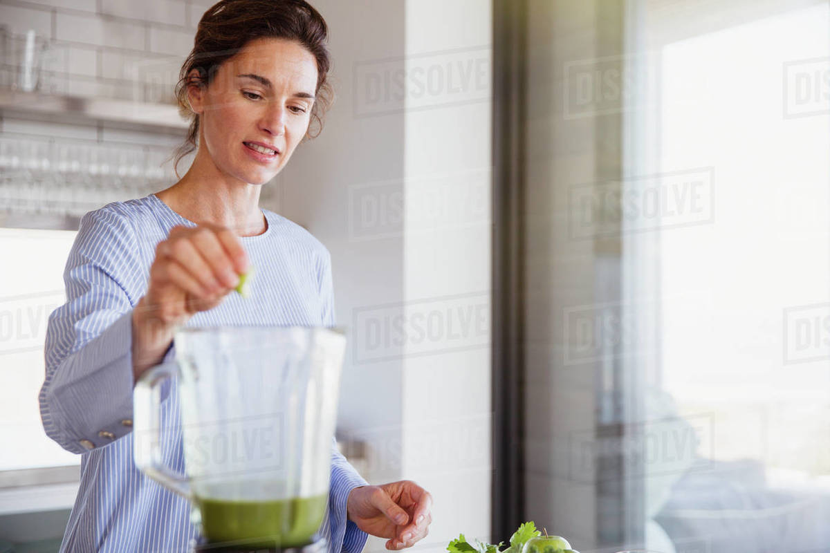 Woman making healthy green smoothie in blender in kitchen - Stock Photo ...