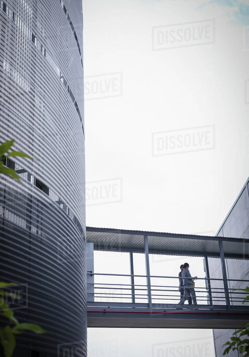 Business people walking on elevated walkway between buildings - Royalty ...