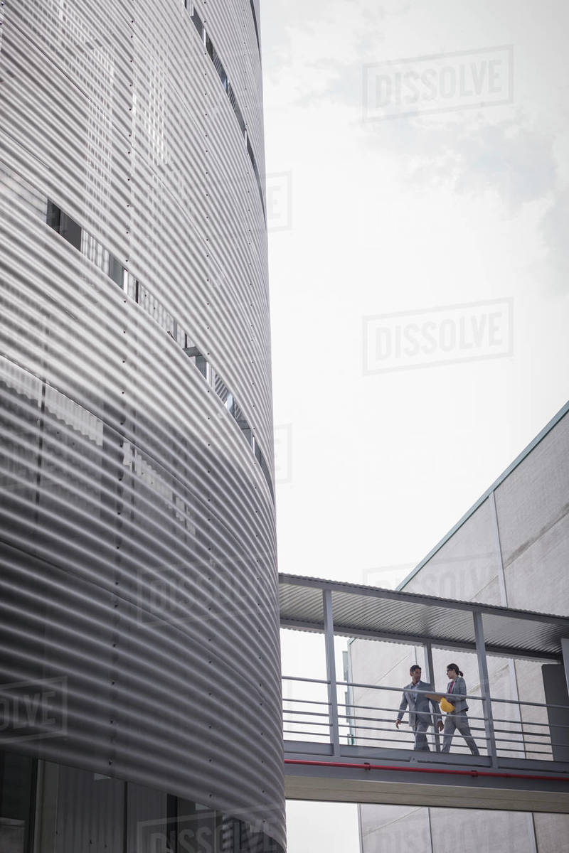 Supervisors walking on elevated walkway between factory buildings ...