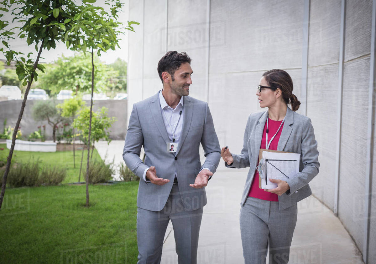 Businessman and businesswoman walking and talking on sidewalk - Stock ...