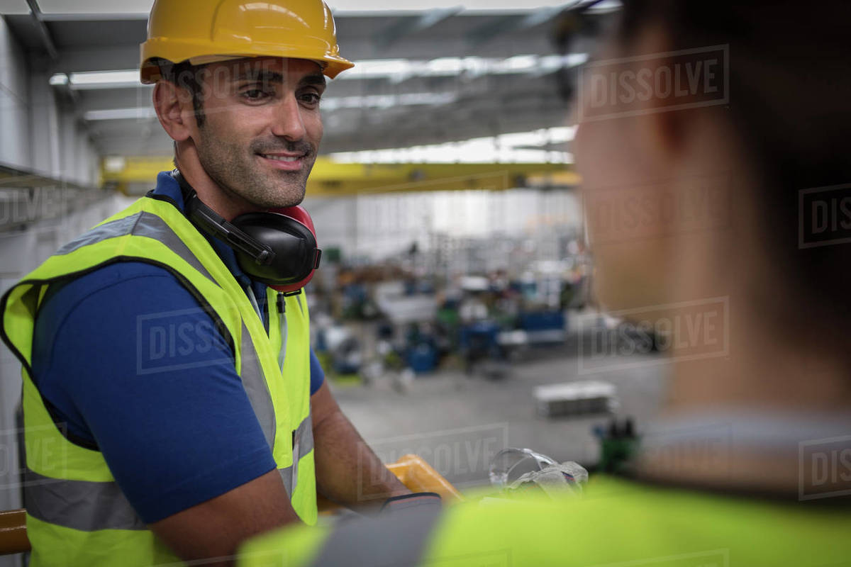 Smiling male supervisor talking to coworker on platform in factory ...