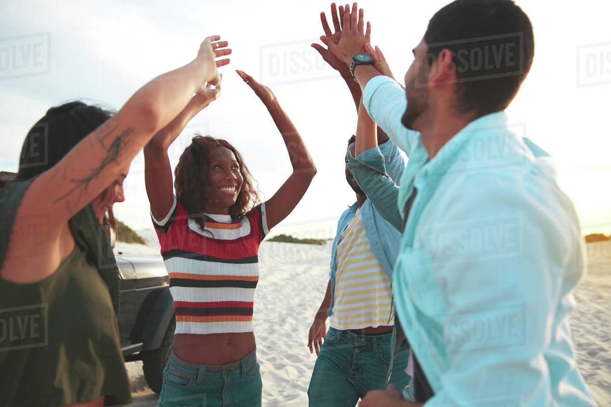 Exuberant young friends high-fiving on beach - Stock Photo - Dissolve