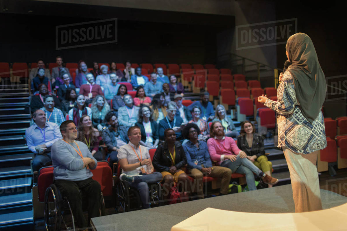 Audience listening to female speaker in hijab talking on stage ...
