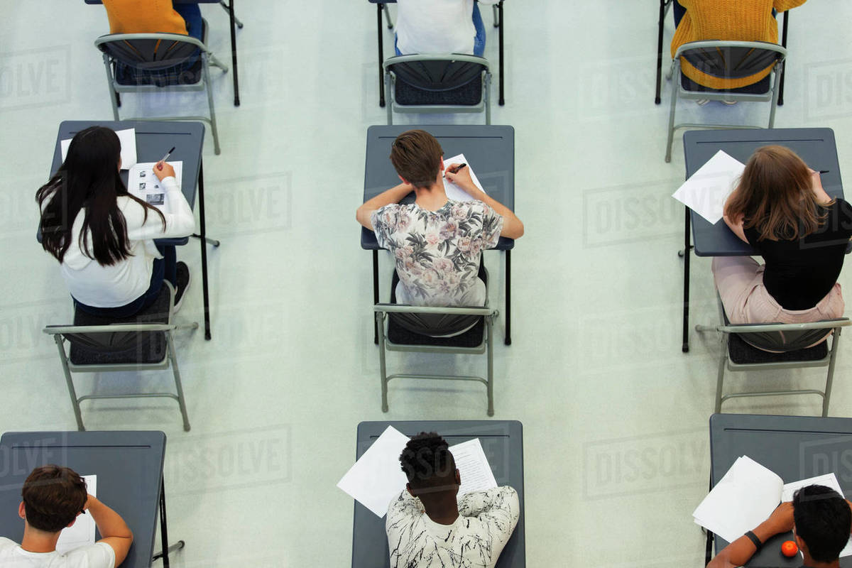 Overhead view high school students taking exam at desks in classroom ...