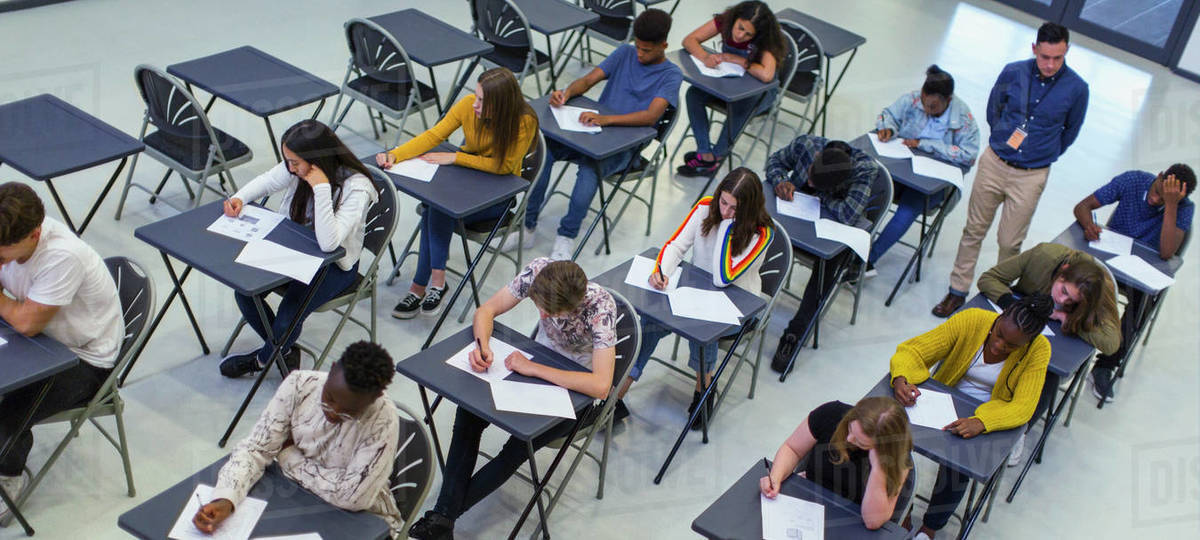 Instructor supervising high school students taking exam at desks ...