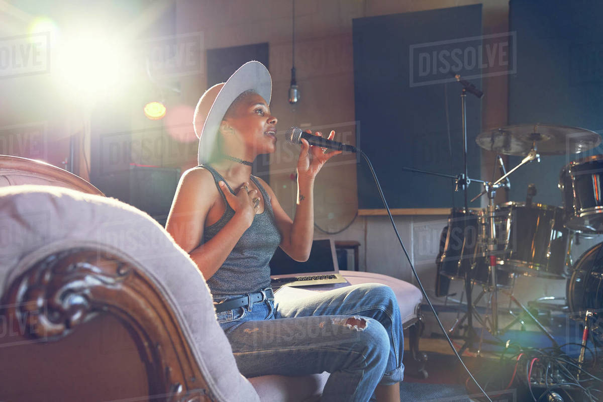 Young female musician singing into microphone in recording studio ...