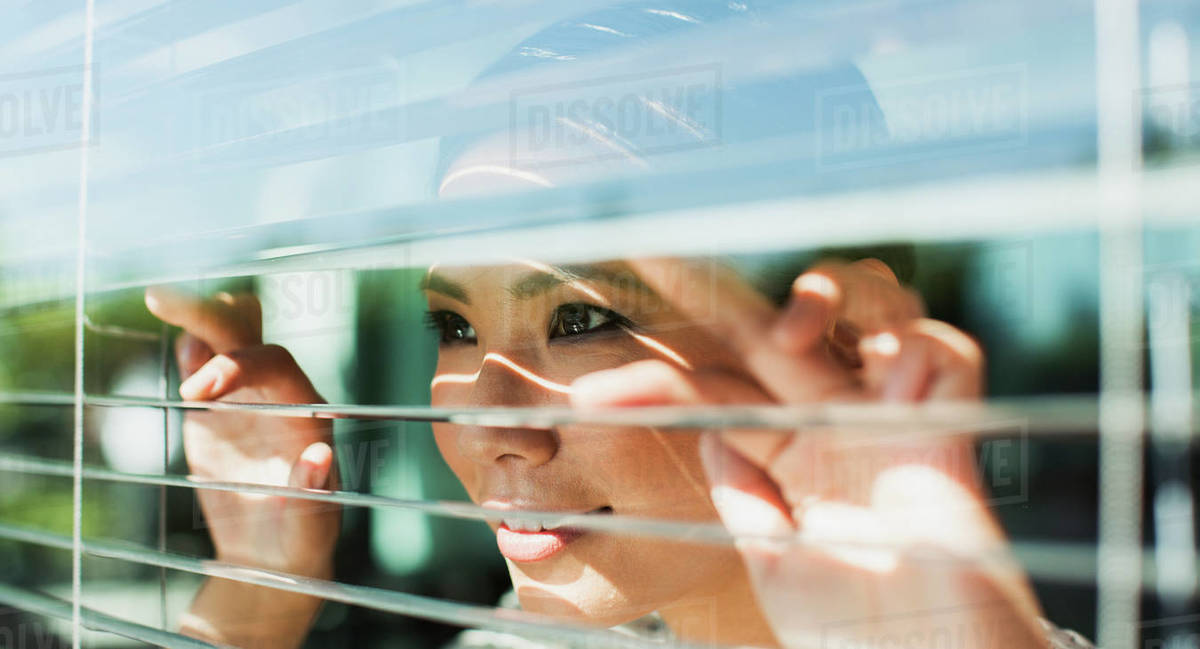 Businesswoman peering through window blinds - Stock Photo - Dissolve