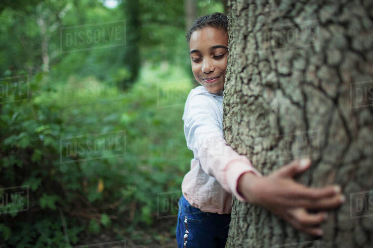 Cute girl hugging tree trunk in woods - Royalty-free Stock Photo | Dissolve