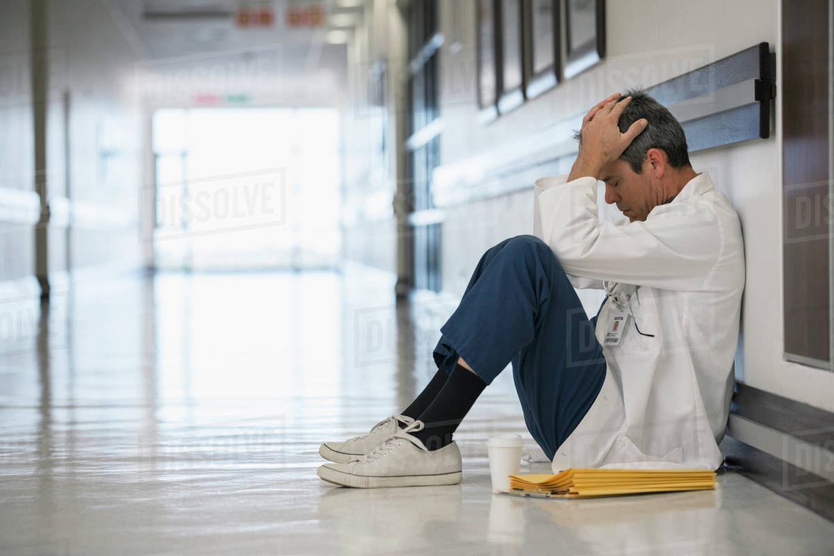 Doctor sitting on floor in hospital corridor with head in hands ...