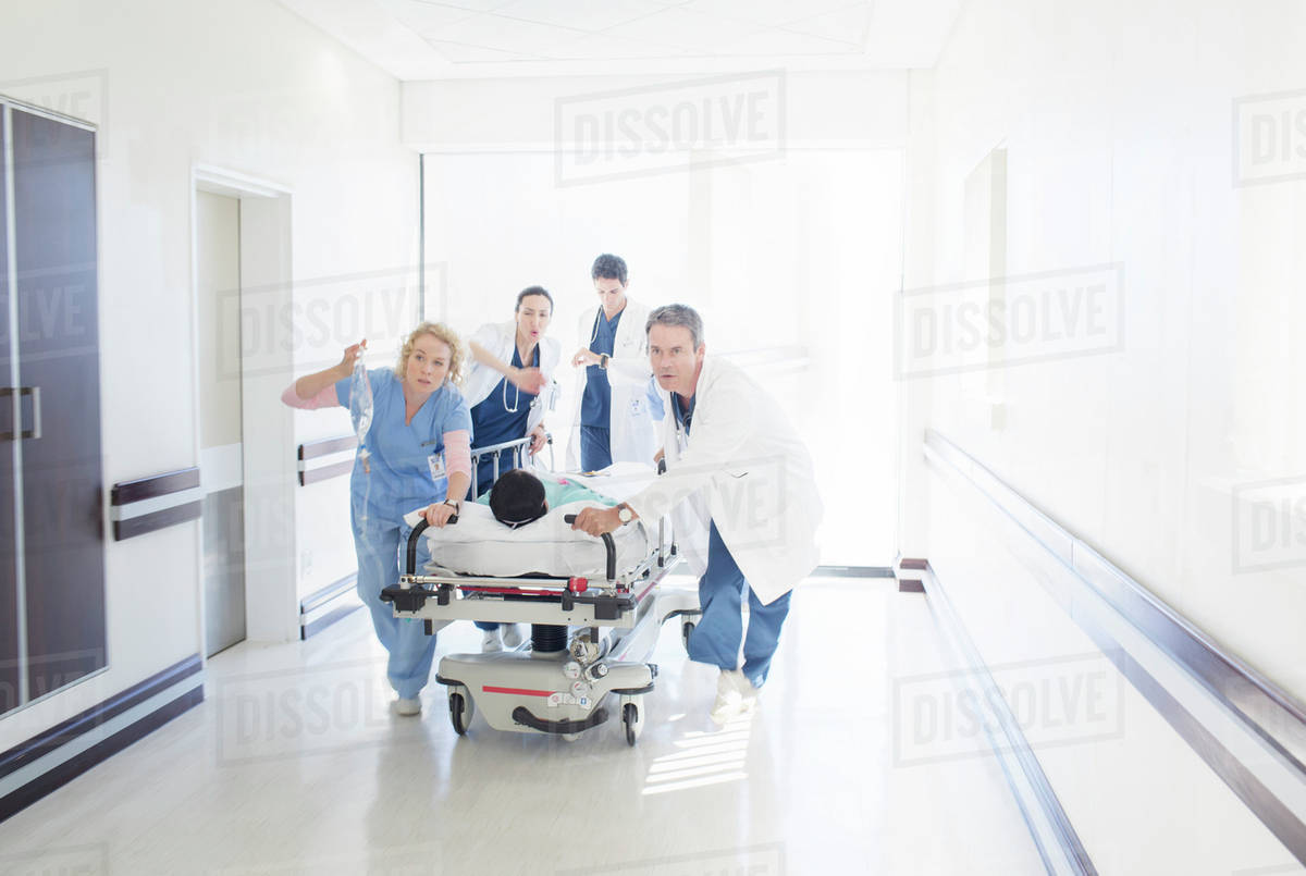 Doctors and nurses rushing patient on stretcher down hospital corridor ...