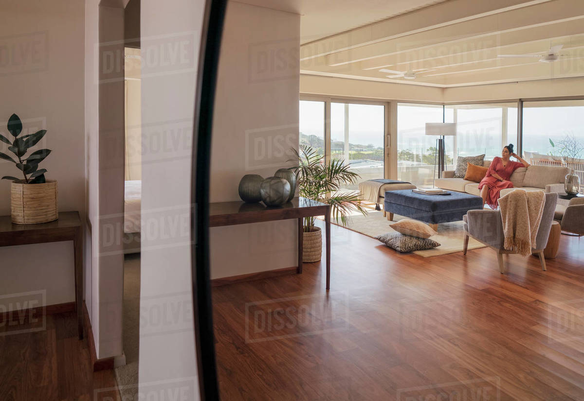 Reflection in mirror of woman relaxing on luxury living room sofa ...