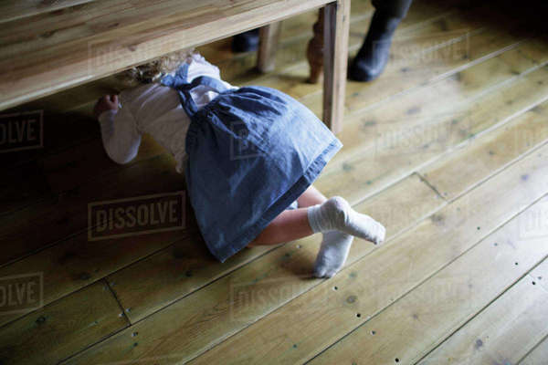 Cute girl in denim dress crawling under wood dining bench - Royalty ...