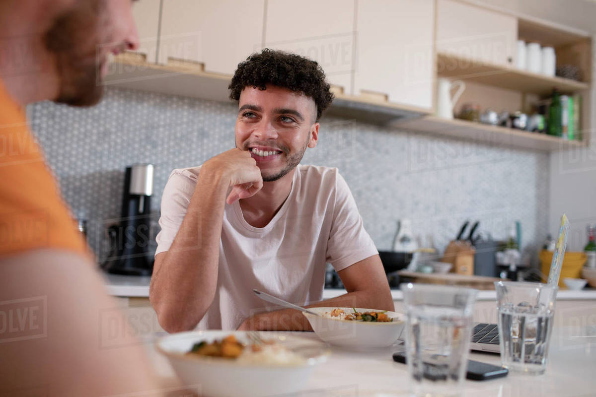 Smiling gay male couple talking and eating in kitchen - Royalty-free ...