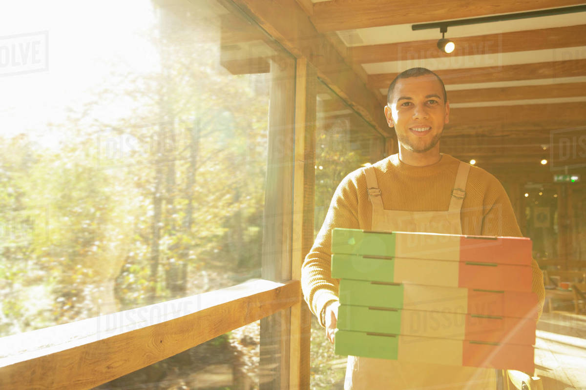 Portrait proud male pizzeria owner with pizza boxes at sunny window ...