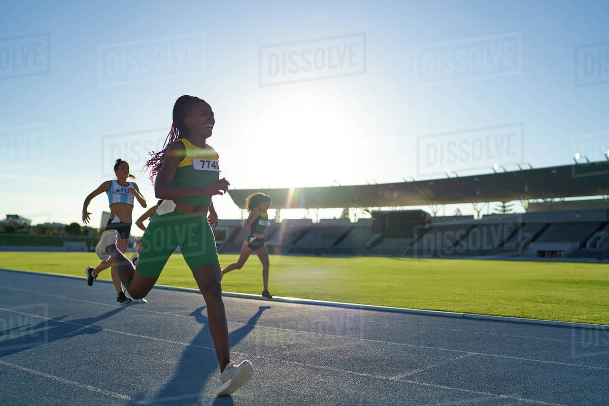 Happy female track and field athlete winning race on sunny track ...