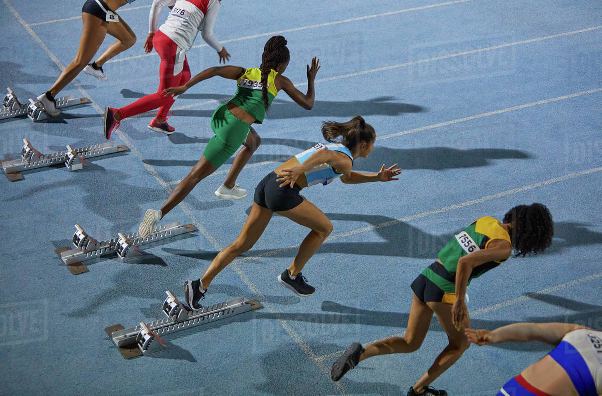 Female track and field athletes taking off from starting blocks ...