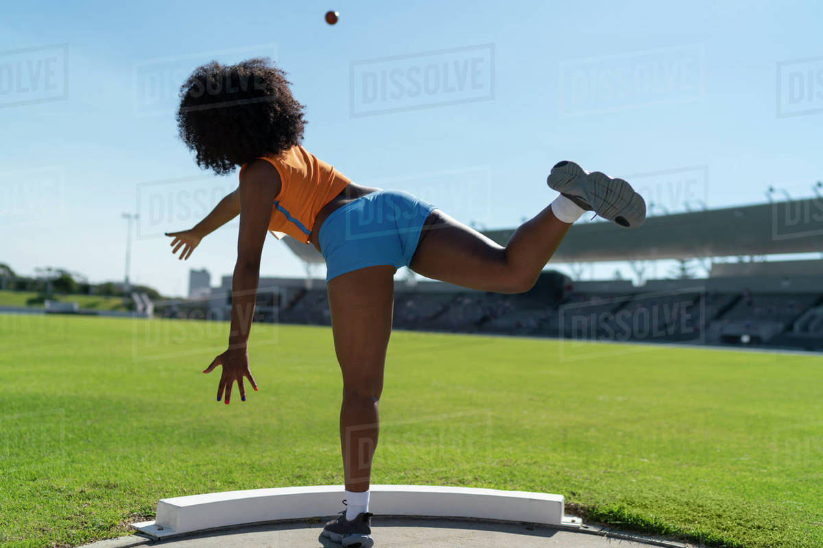 Female track and field athlete throwing shot put in sunny infield ...