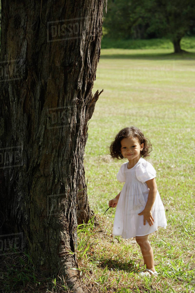 Little girl standing by tree, smiling - Royalty-free Stock Photo | Dissolve