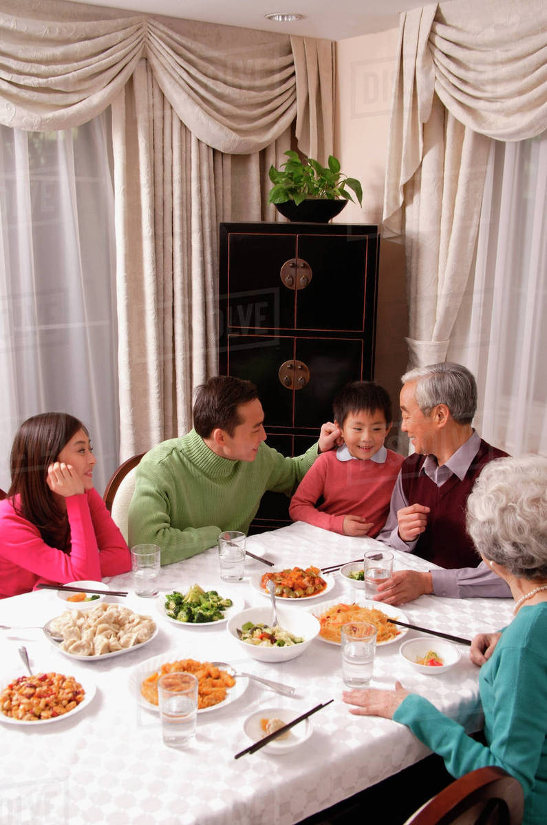Family at dinner table having traditional food, boy standing next to ...