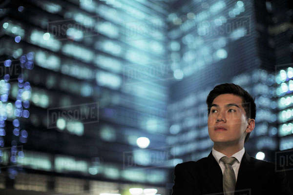 Man wearing a suit standing in front of lit buildings at night - Stock ...
