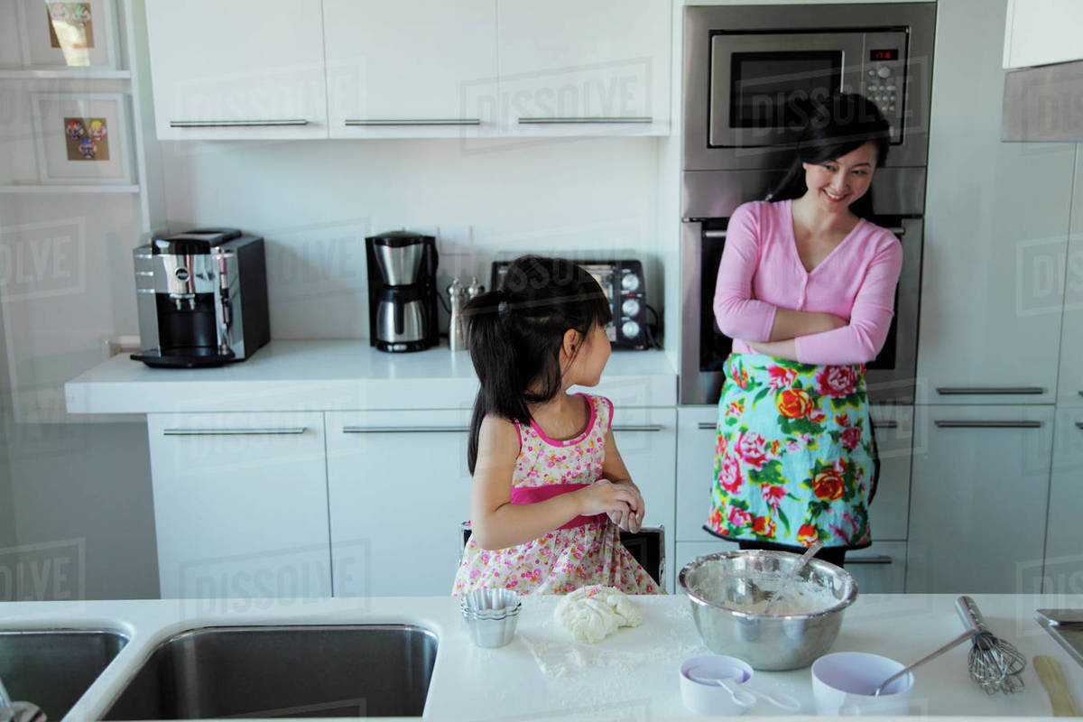 Mother watching her daughter cook in the kitchen - Stock Photo - Dissolve