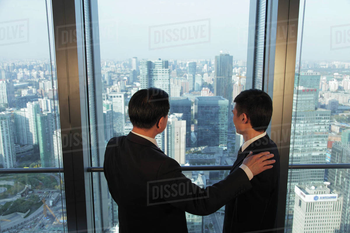 Two men talking in front of window with a view of the city of Beijing ...