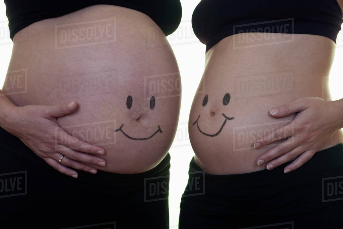 Two pregnant women with smiley faces on their bellies, midsection ...
