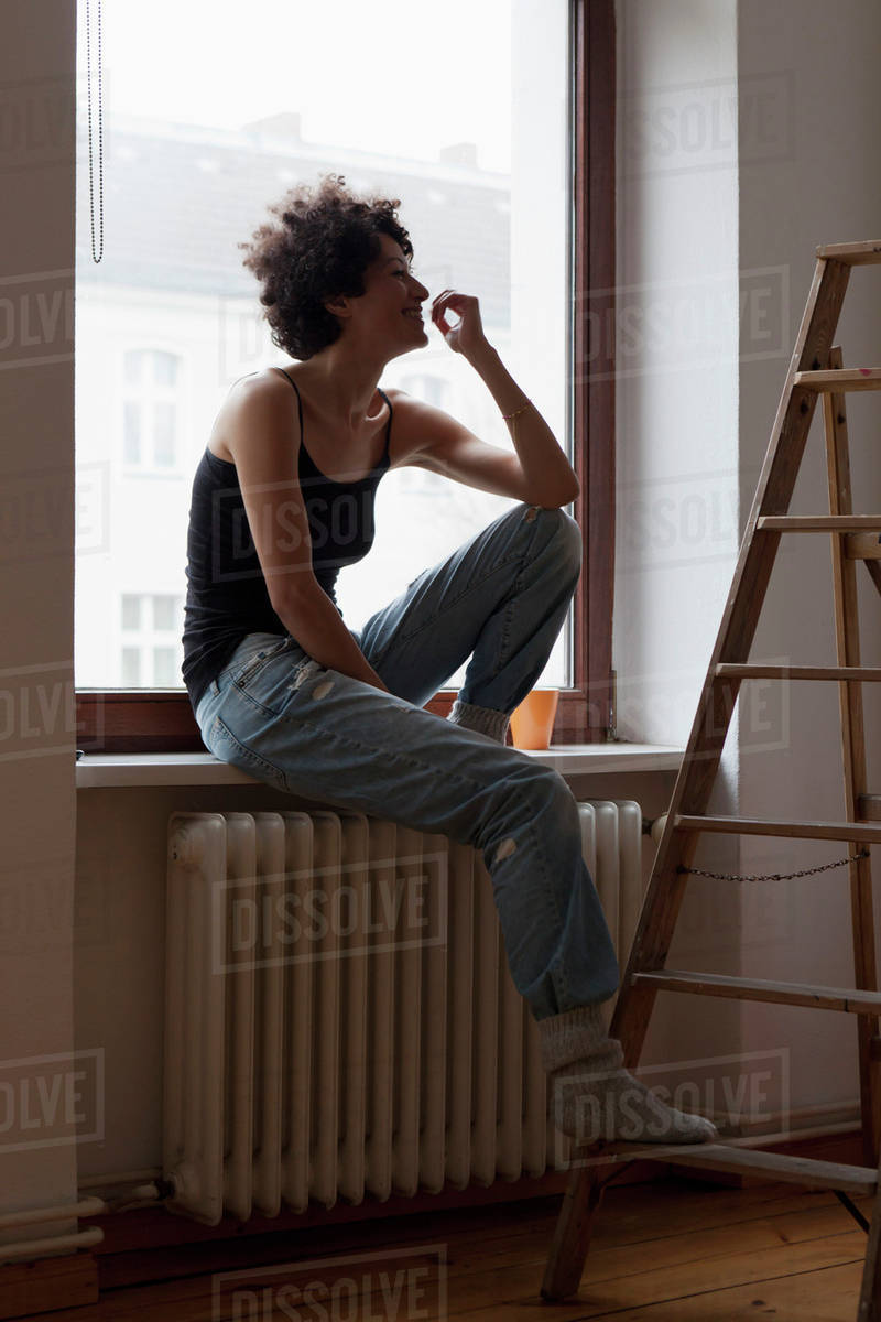 A woman sitting on a window sill and resting her foot on a ladder ...