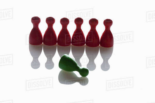 A row of red game pieces with a green piece knocked over in front of ...