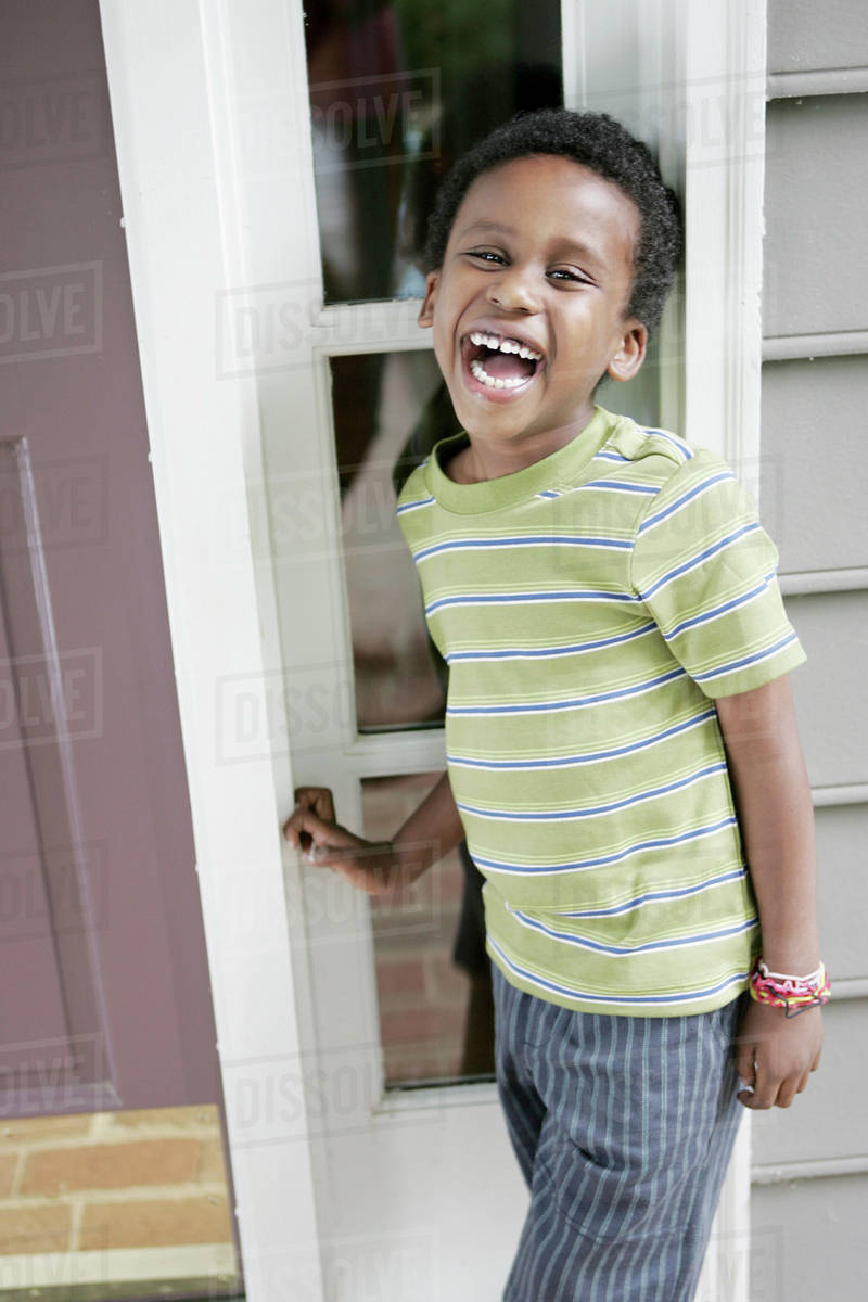 A cheerful laughing boy standing at the front door of his house - Stock ...