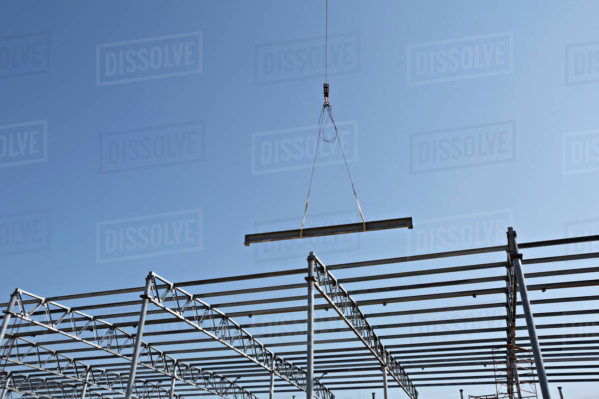 Crane lowering steel beam towards construction frame - Royalty-free ...
