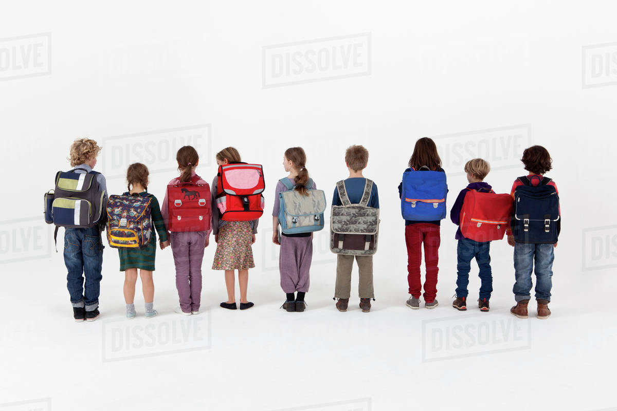 A group of school children wearing backpacks and standing in a row ...