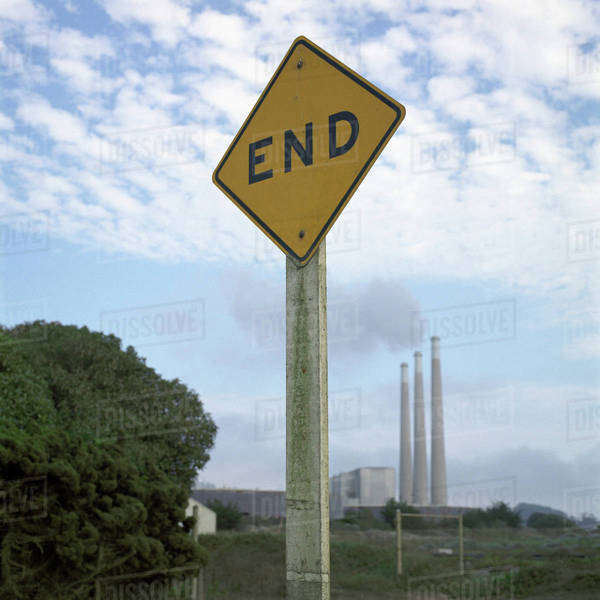A dead end road sign in foreground, smoke stacks emitting smoke in ...