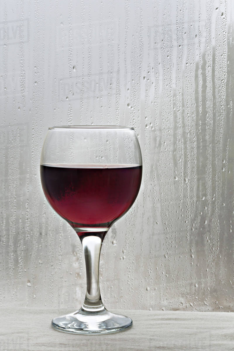 Glass of red wine by rain covered window - Stock Photo - Dissolve